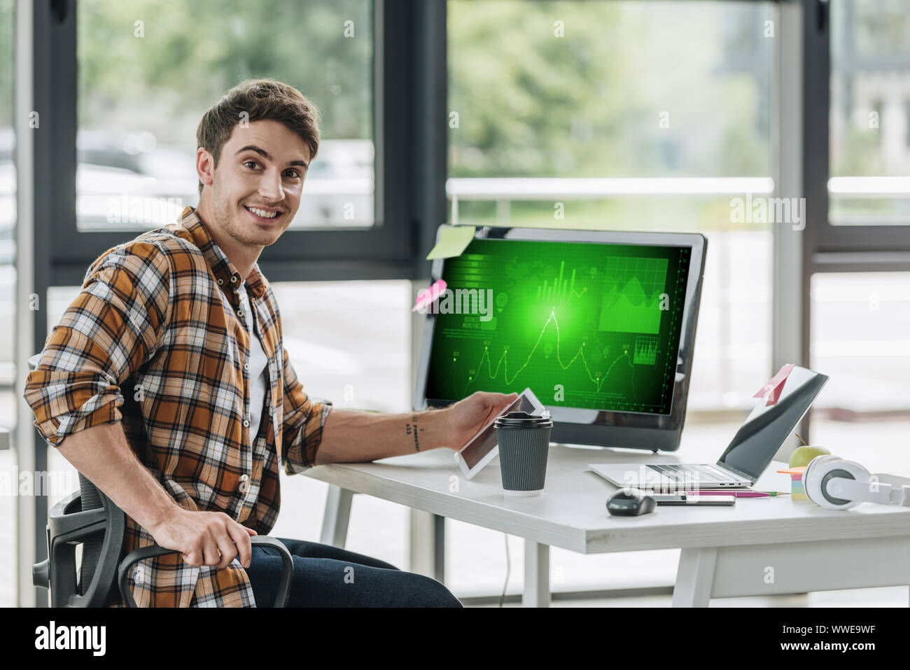 cheerful programmer smiling at camera while sitting near computer ...