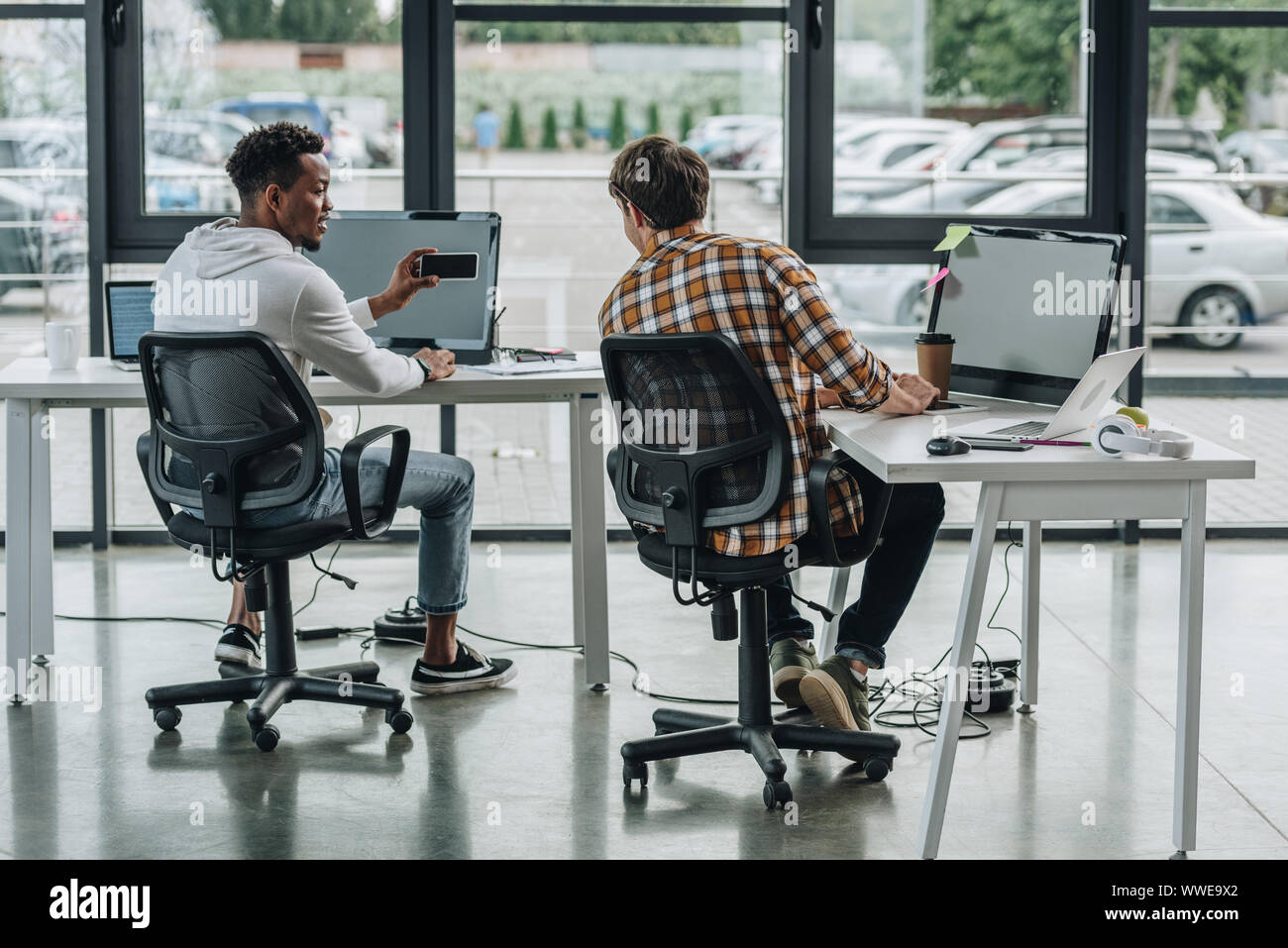 back view of young programmer sitting near african american colleague ...