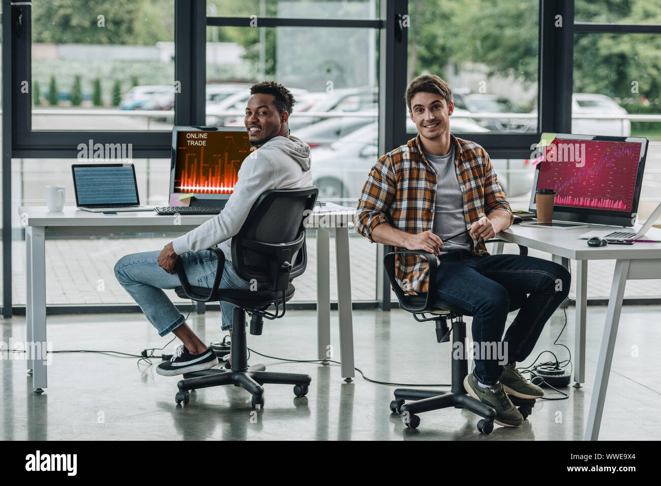 two cheerful multicultural programmers smiling at camera while sitting ...