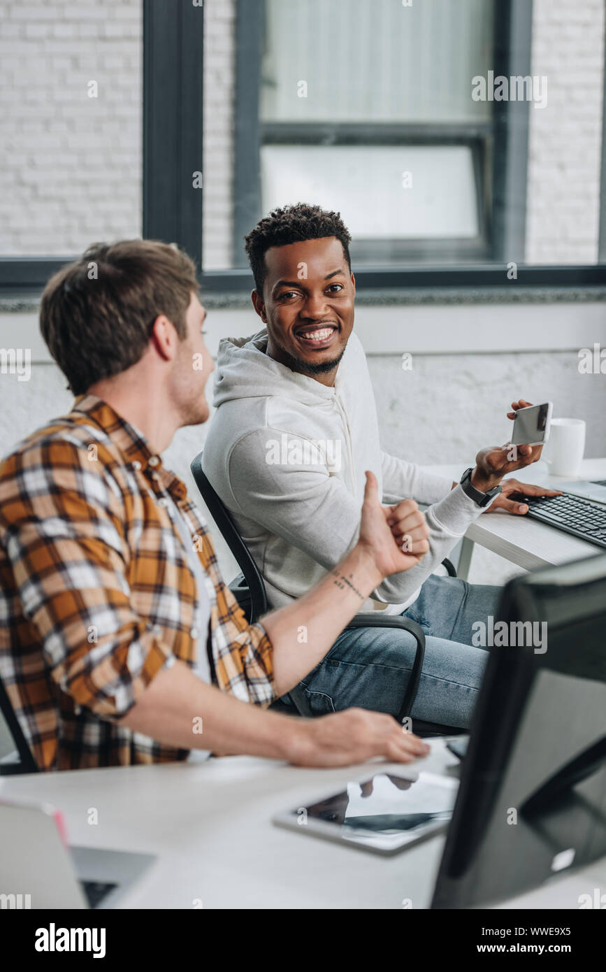 cheerful african american programmer holding smartphone and looking at ...