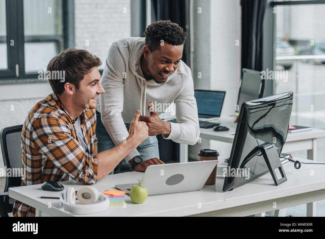 two cheerful multicultural programmers showing thumbs up while looking ... two cheerful multicultural programmers showing thumbs up while looking ...