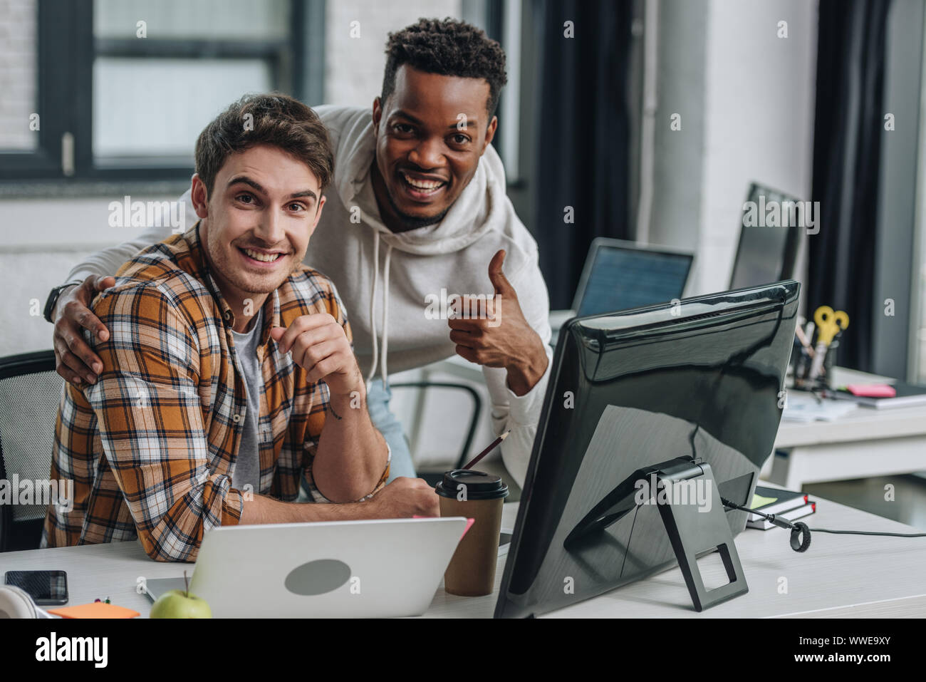 two cheerful multicultural programmers looking at camera and showing ... two cheerful multicultural programmers looking at camera and showing ...