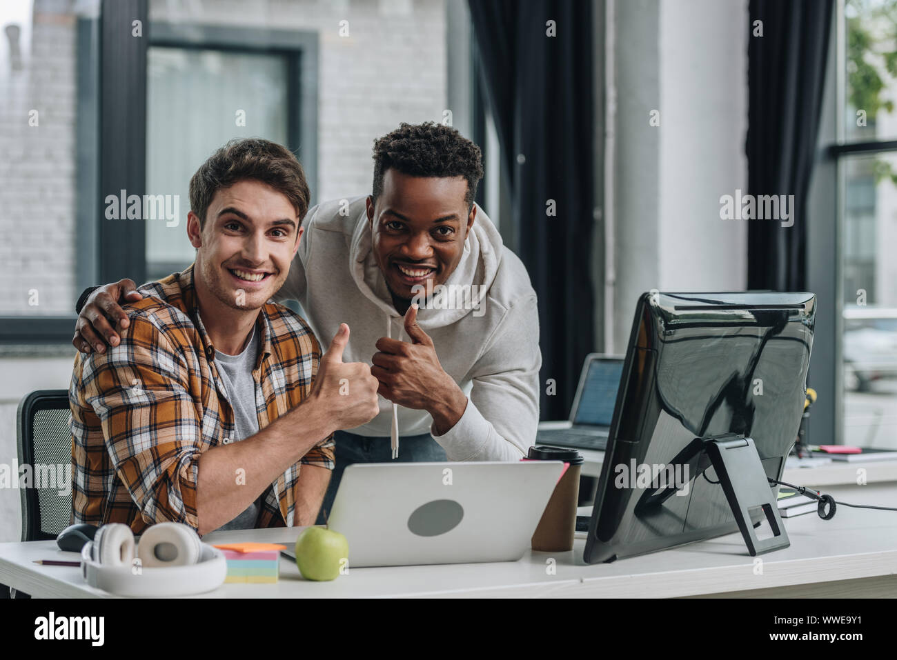 two young multicultural programmers smiling at camera and showing ... two young multicultural programmers smiling at camera and showing ...