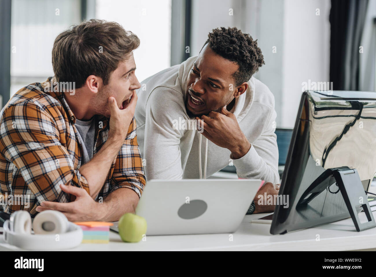 two shocked multicultural programmers looking at each other while ...