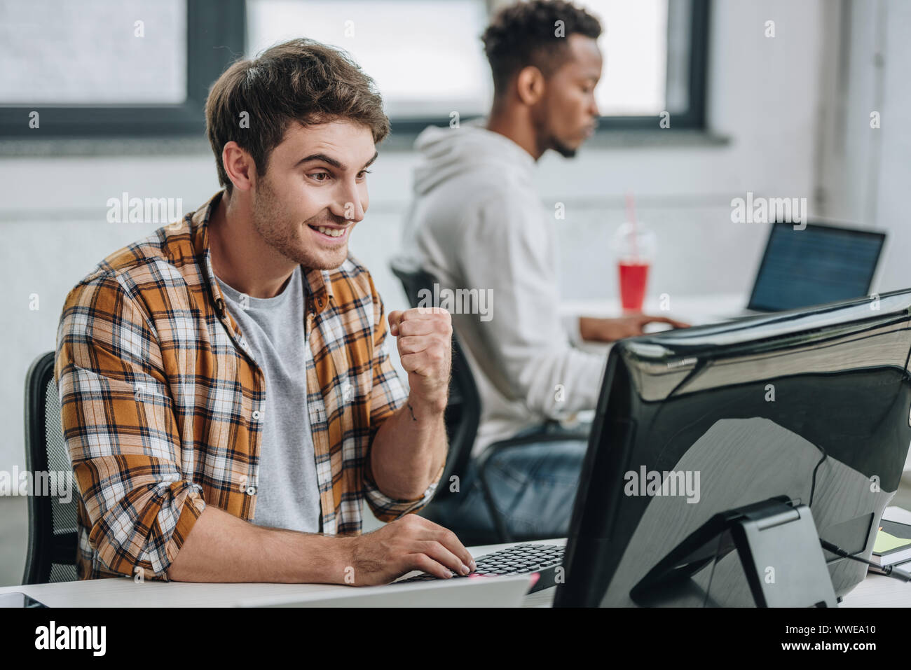 cheerful programmer showing winner gesture while working near african ...