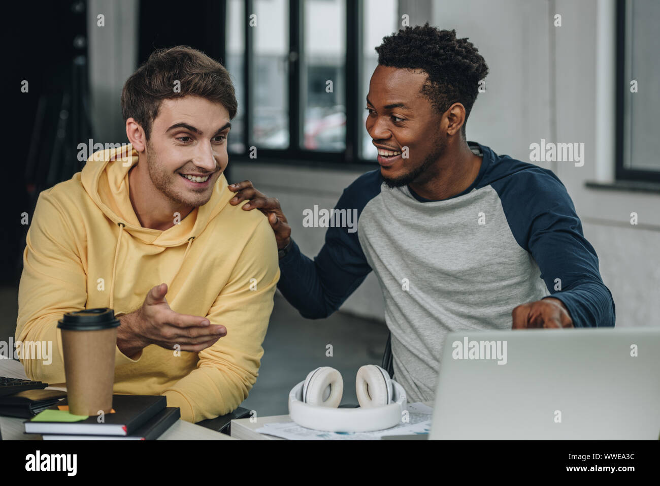 happy young programmer pointing at computer monitor while sitting near ...