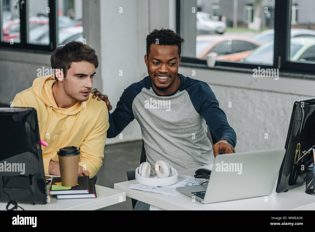 cheerful african american programmer pointing at laptop while sitting ...