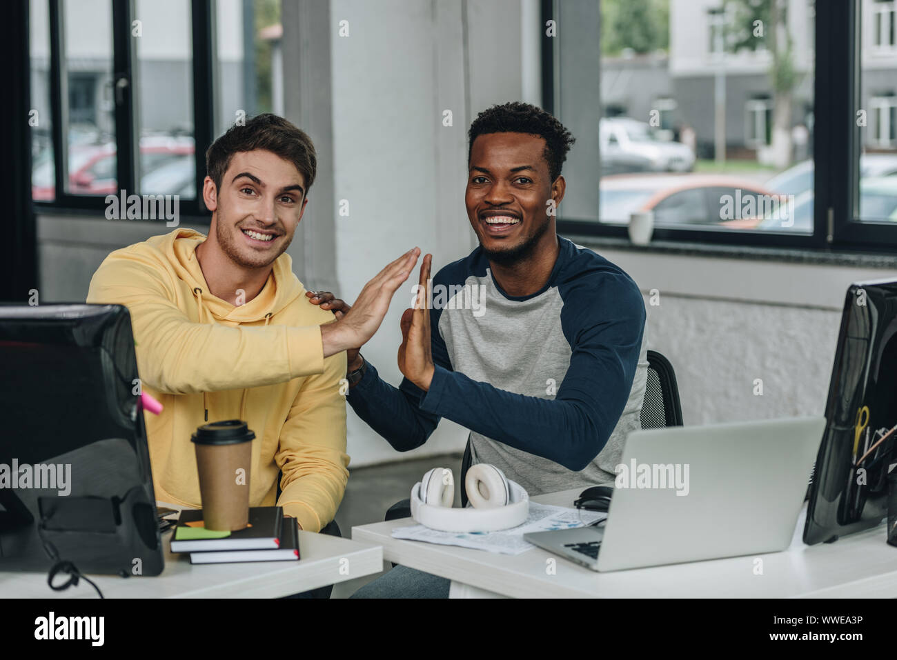 two multicultural programmers giving high five and smiling at camera in ... two multicultural programmers giving high five and smiling at camera in ...