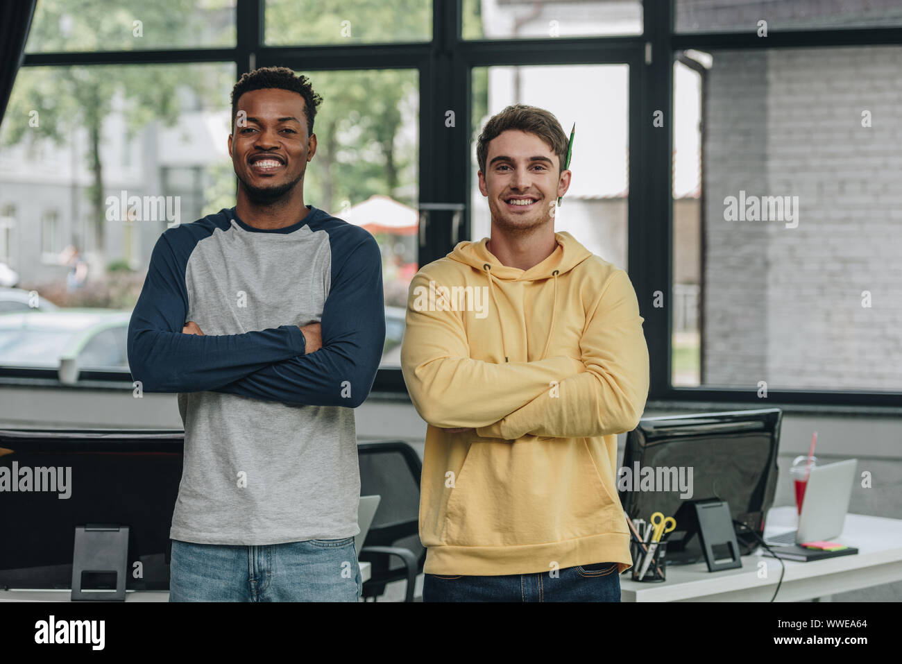 two cheerful multicultural programmers standing with crossed arms and ... two cheerful multicultural programmers standing with crossed arms and ...