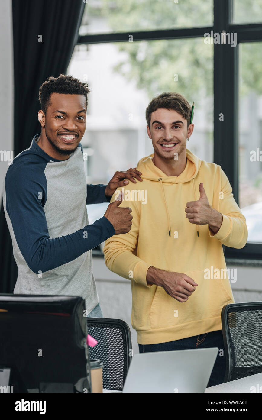 two happy multicultural programmer showing thumbs up while smiling at ...