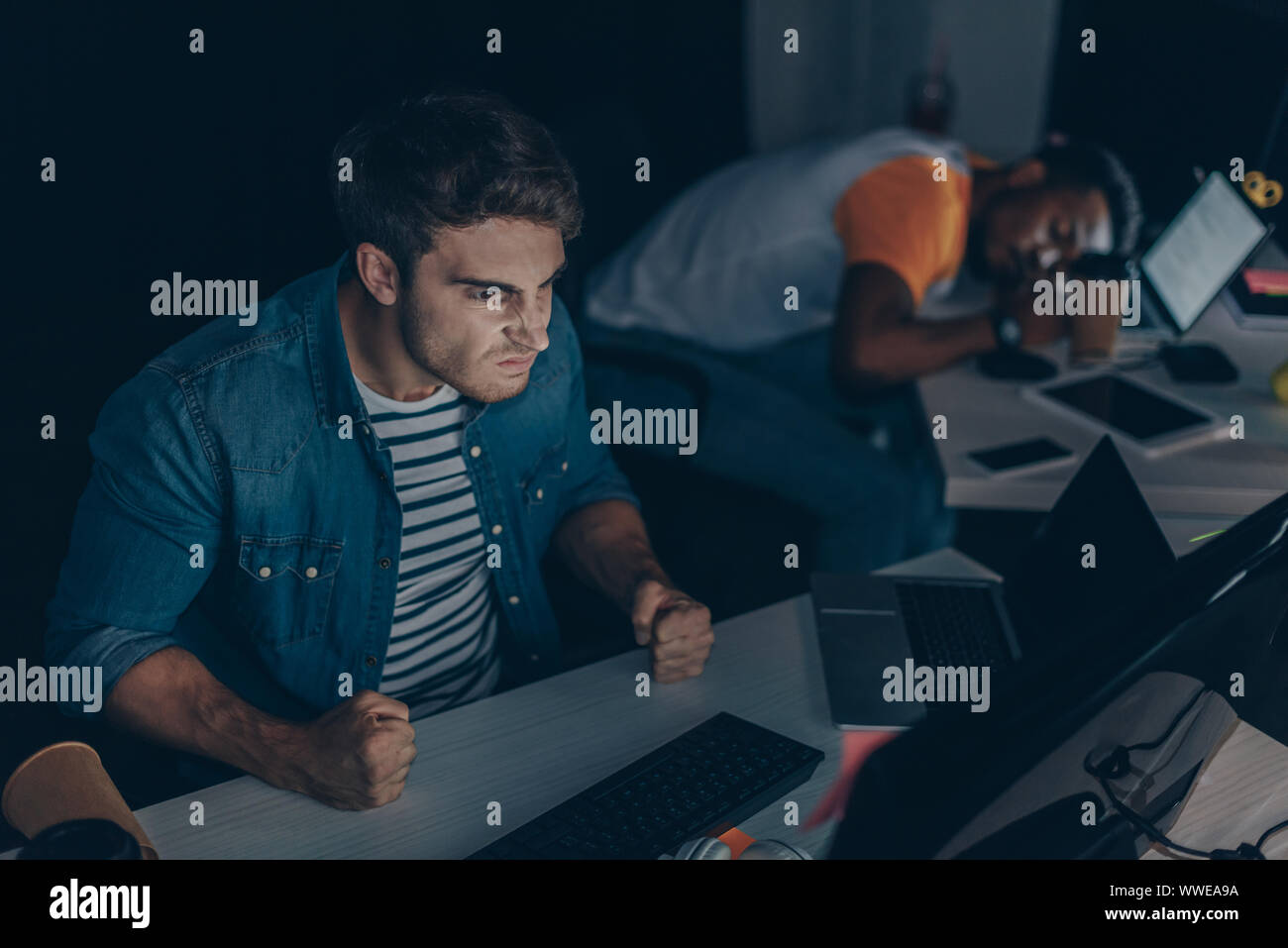 irritated programmer gesturing while working at night in office near ...