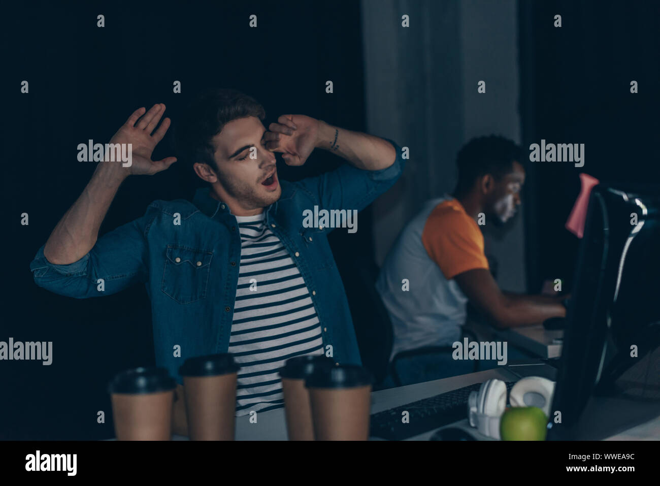 selective focus of young programmer yawning while sitting near working ...