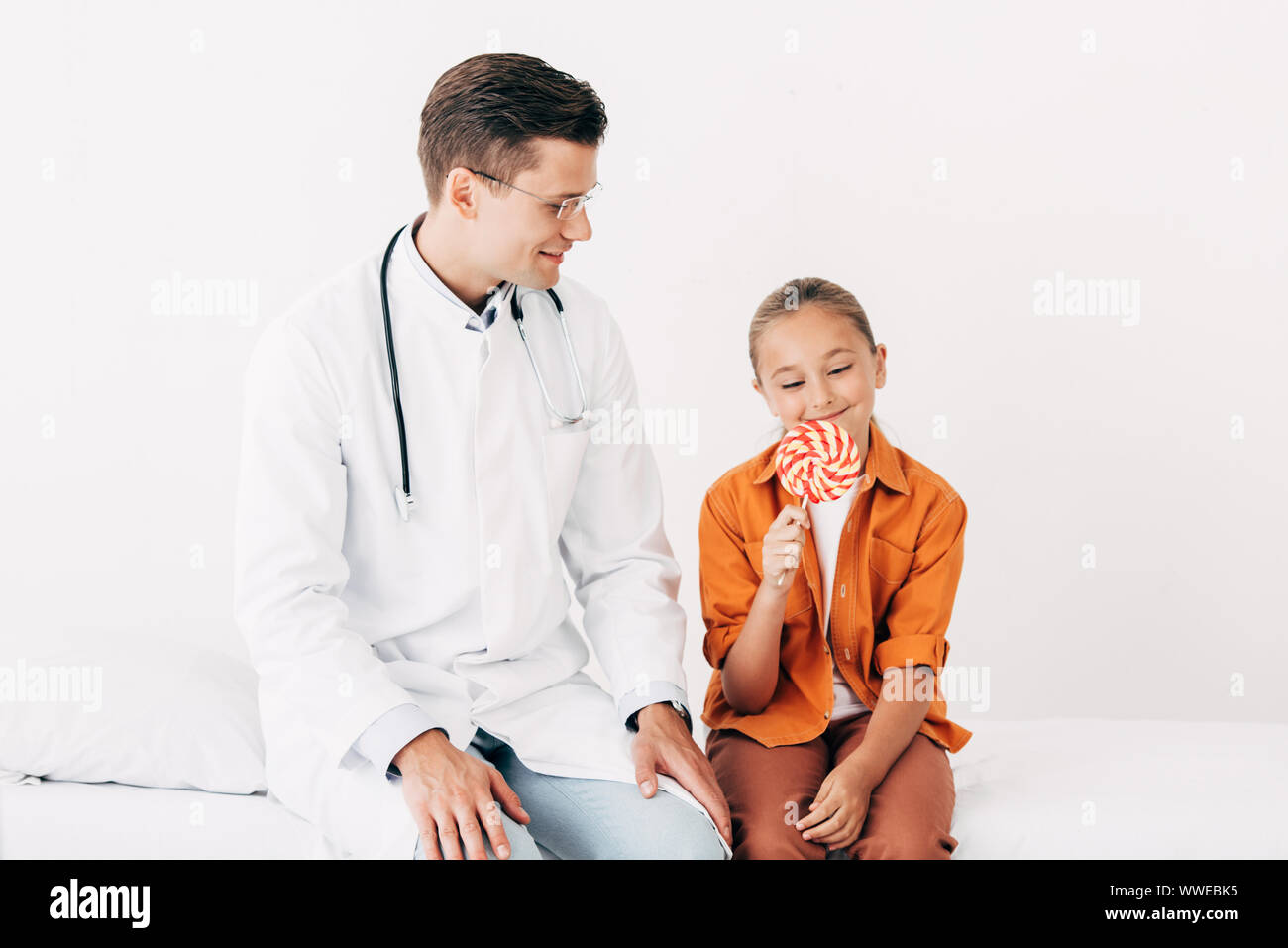 smiling pediatrist in white coat and child with lollipop sitting on ...