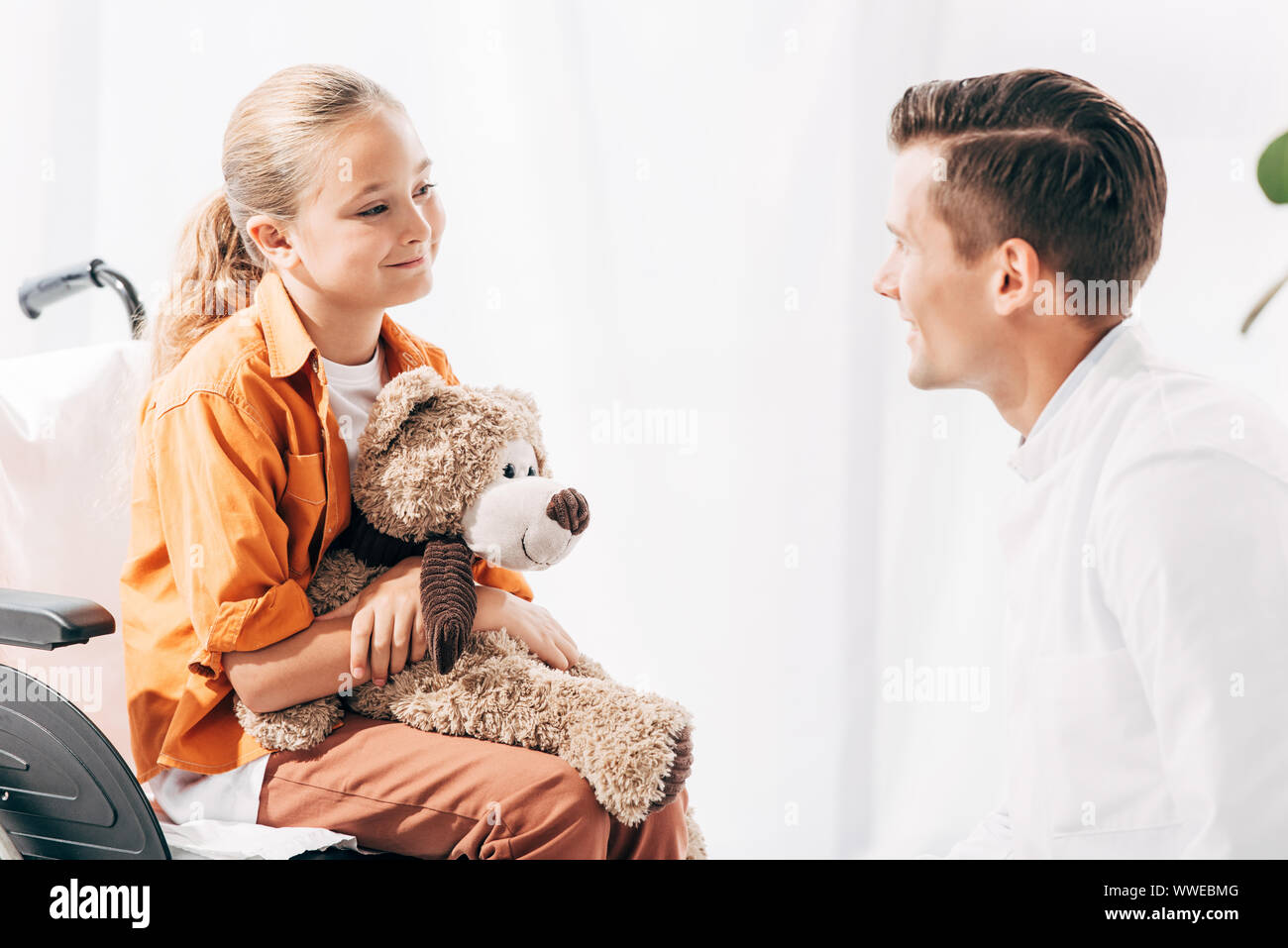 pediatrist and kid with teddy bear on wheelchair looking at each other ...