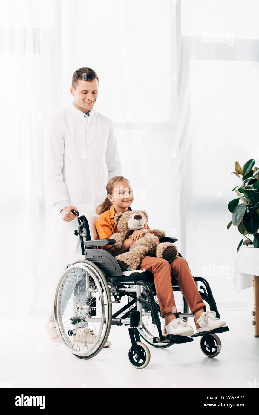 full length view of pediatrist in white coat and kid with teddy bear on ...