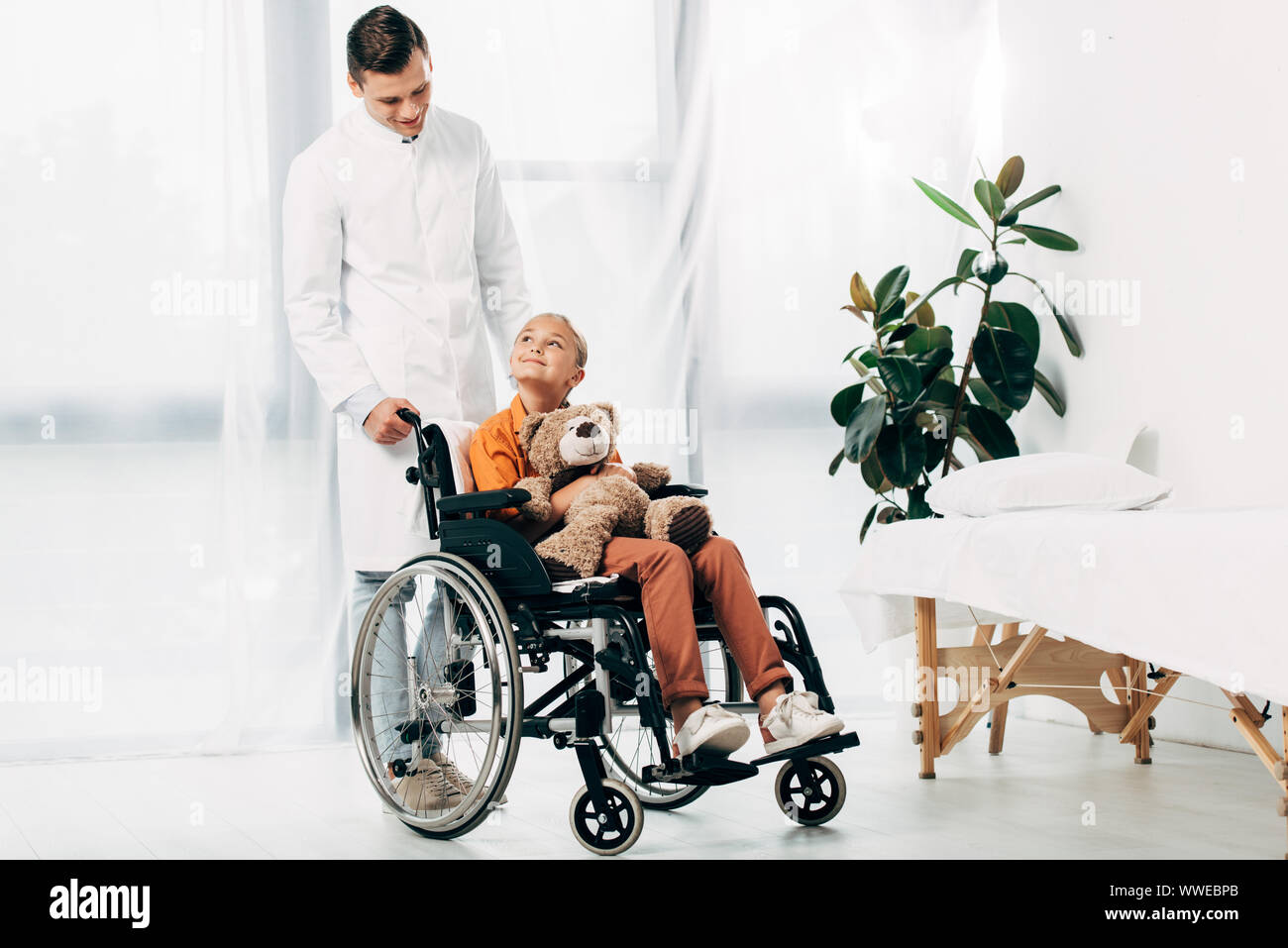 full length view of pediatrist in white coat and kid with teddy bear on ...