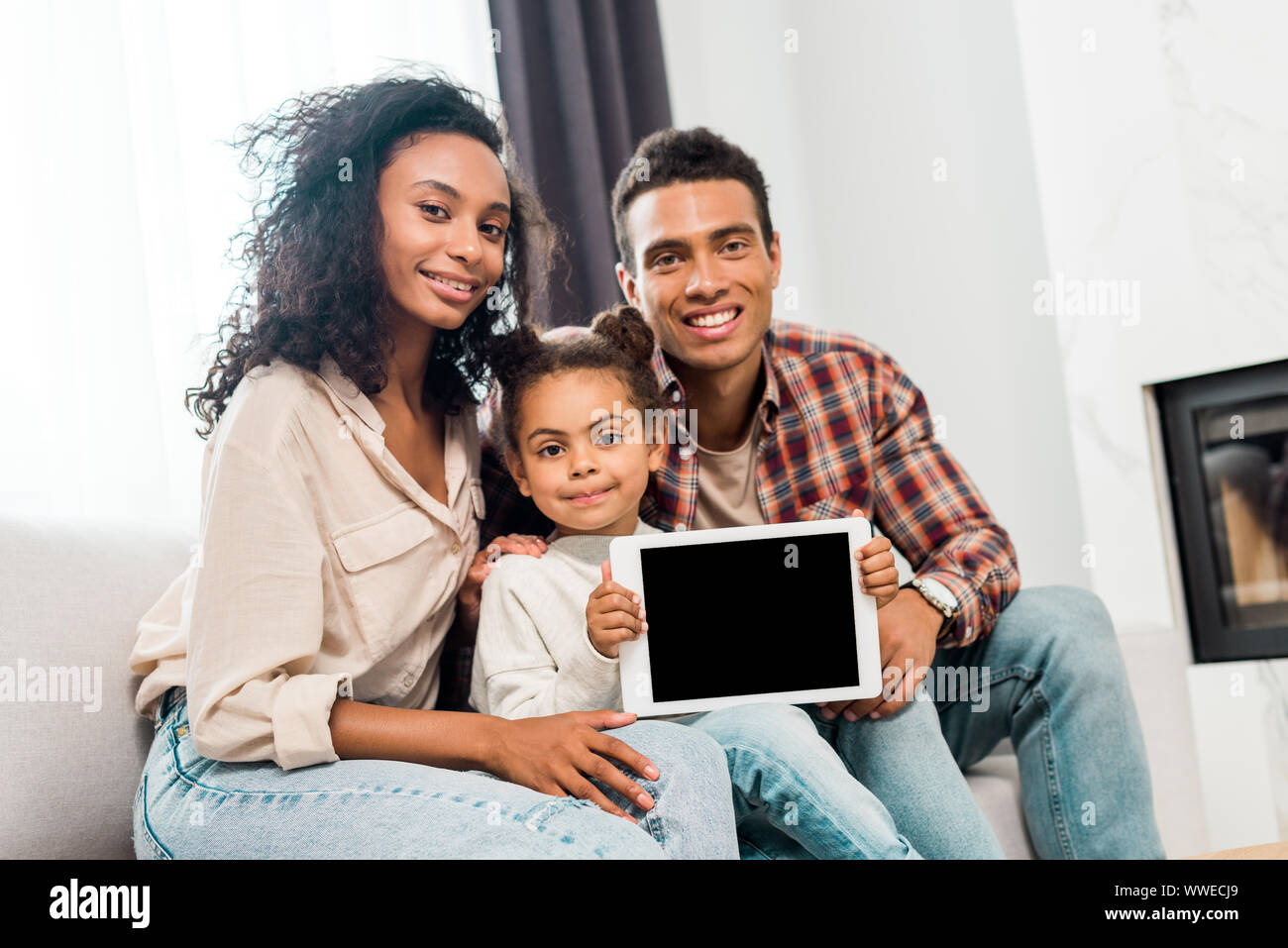 kid showing at camera digital tablet while african american parents ...