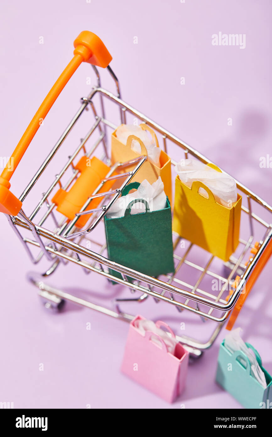 decorative shopping cart with colorful paper bags on violet background ...