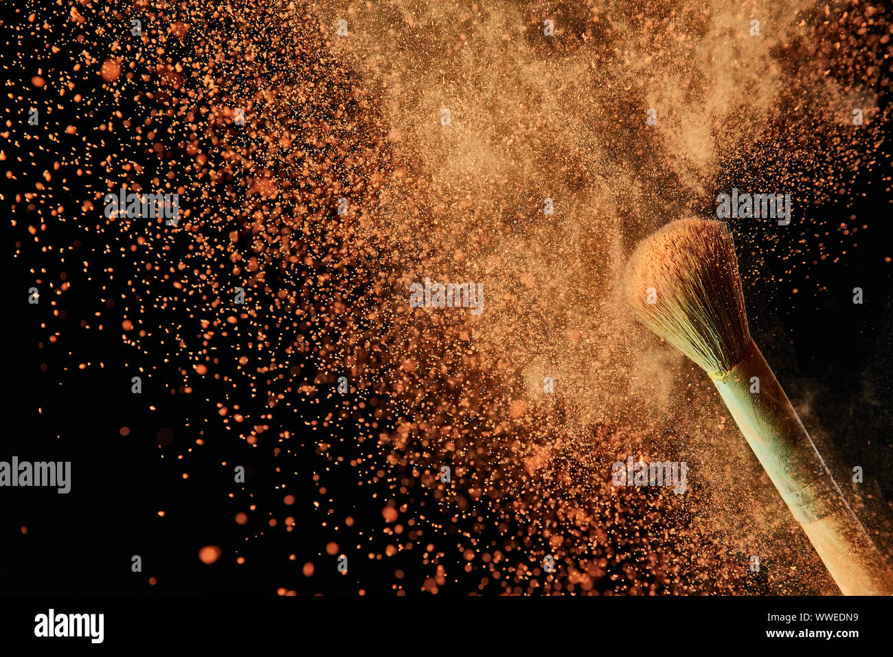 cosmetic brush with colorful orange powder explosion on black ...