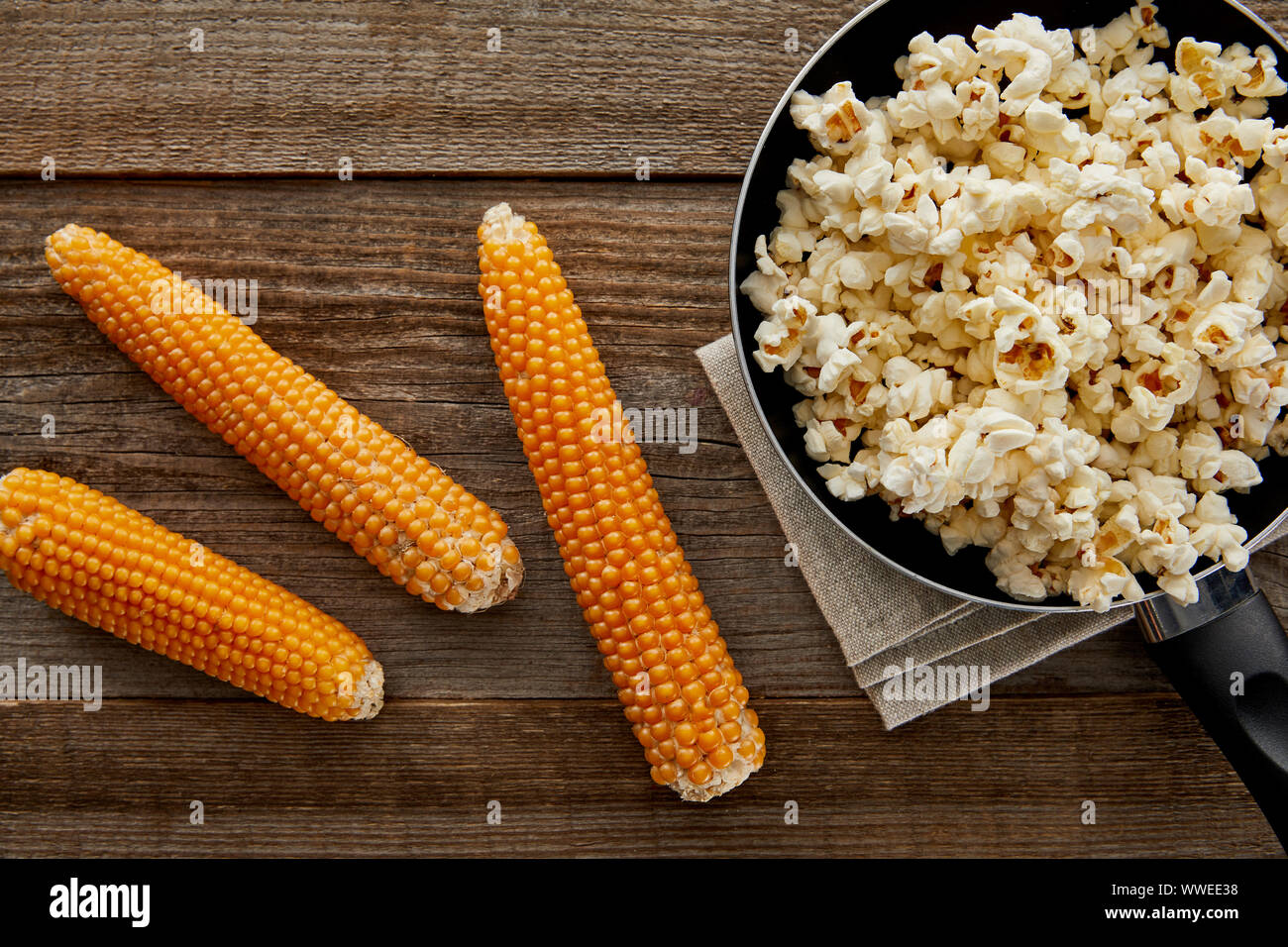 top view of delicious popcorn in frying pan near corn on wooden ...