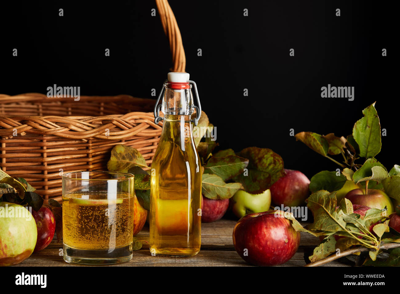 bottle and glass of homemade cider near wicker basket and apples ...