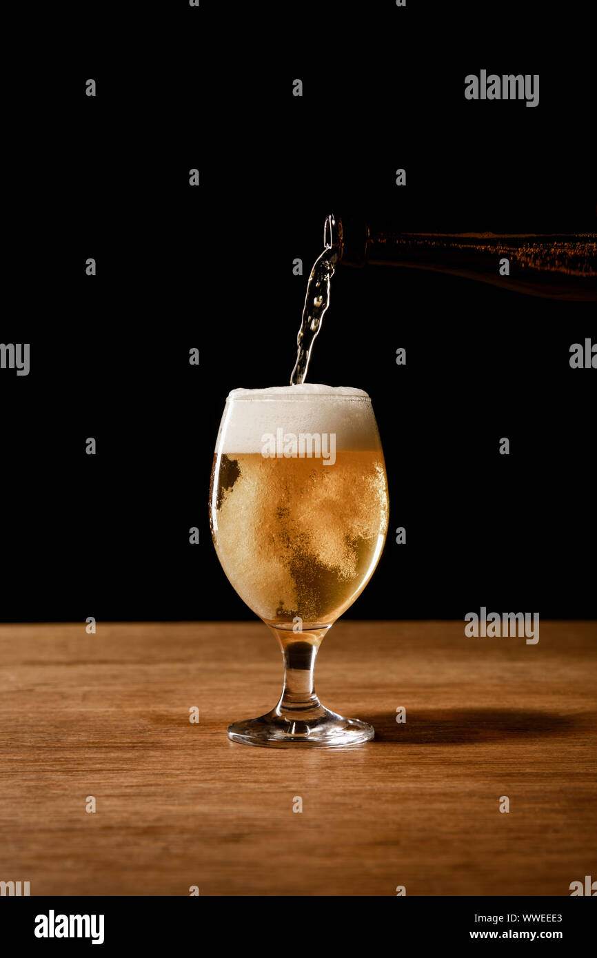 beer pouring from bottle in glass isolated on black Stock Photo - Alamy