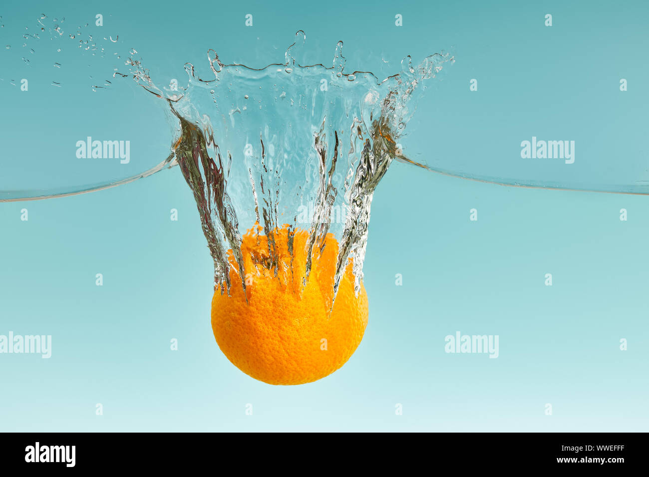 tasty fresh orange falling in water with splash on blue background ...
