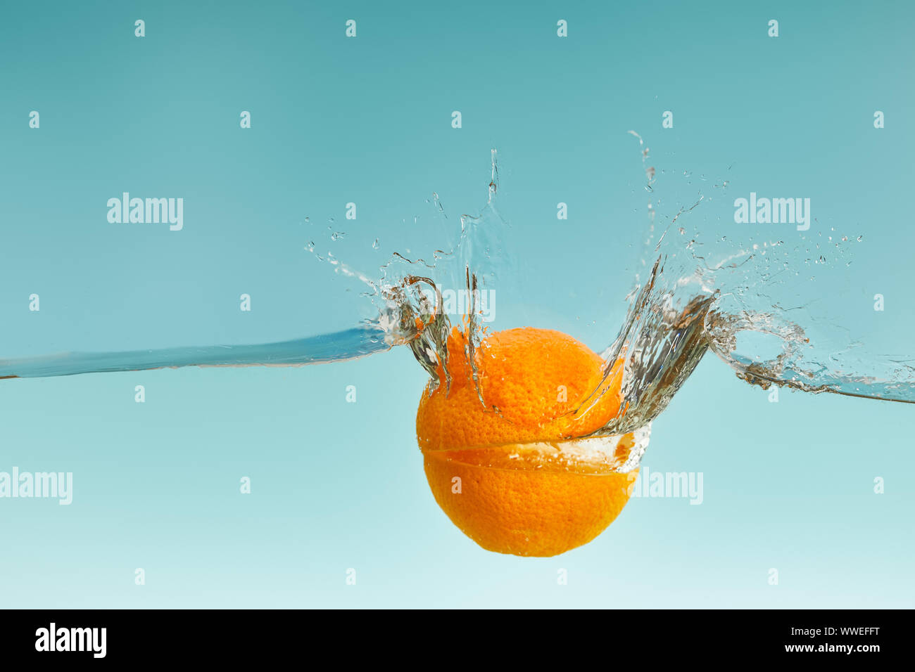 cut orange falling in water with splashes on blue background Stock ...