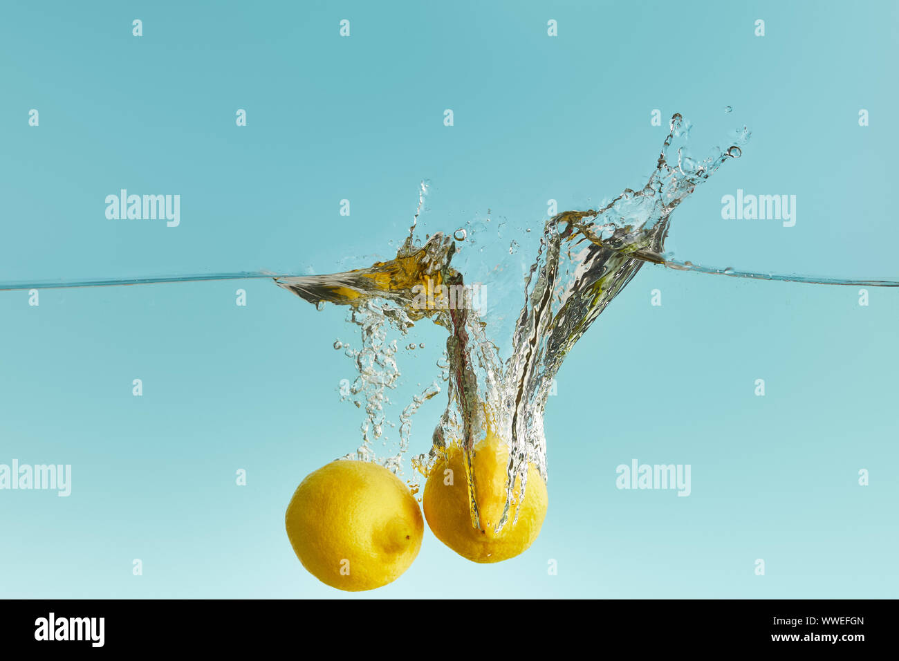 whole ripe lemons falling deep in water with splash on blue background ...