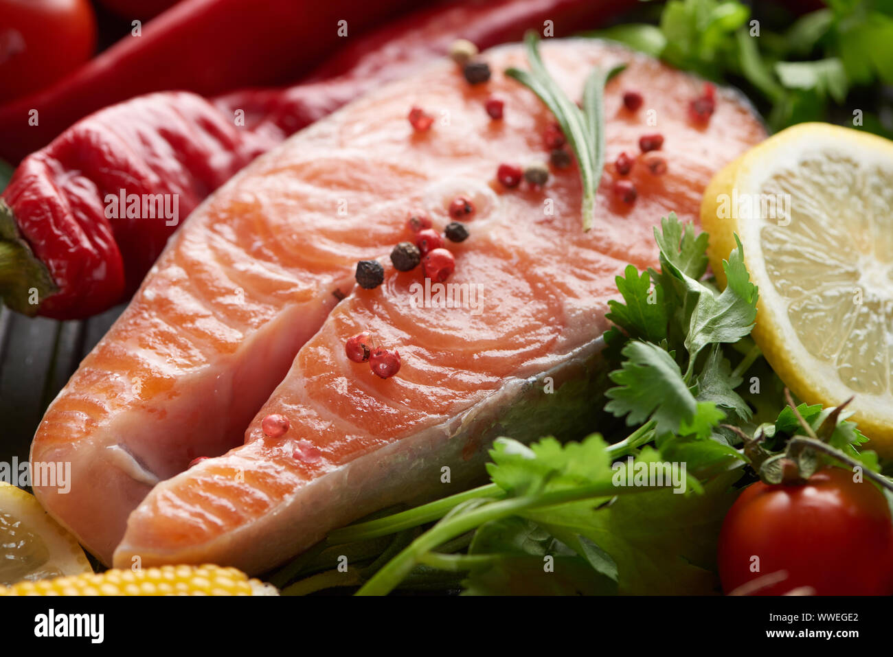 close up view of raw salmon steak with spices, vegetables and greenery ...