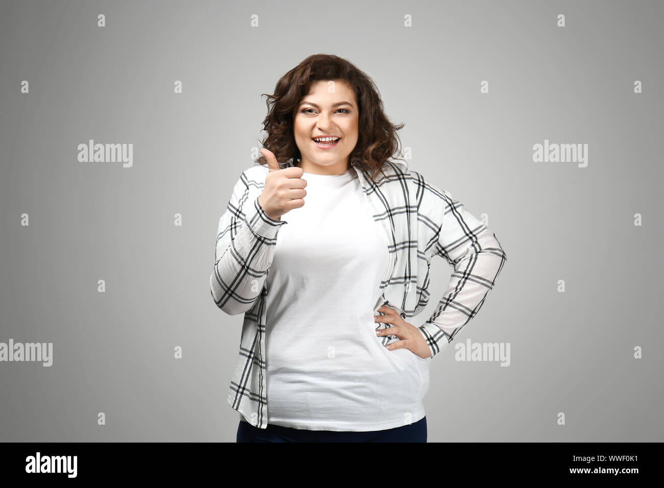 Happy overweight woman showing thumb-up on light background Stock Photo ...