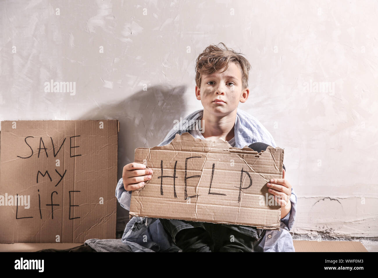 Homeless little boy begging for help indoors Stock Photo - Alamy