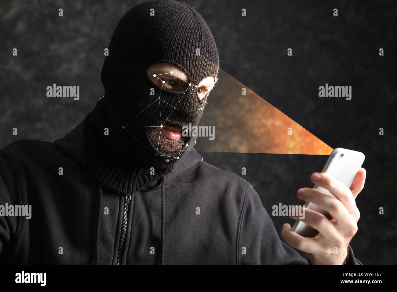 Male hacker in mask holding smartphone protected with facial ...