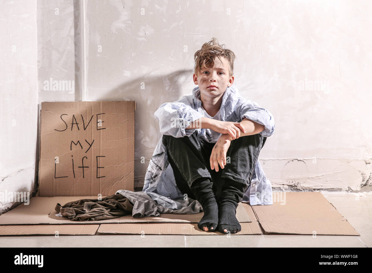 Homeless little boy sitting on floor near wall Stock Photo - Alamy