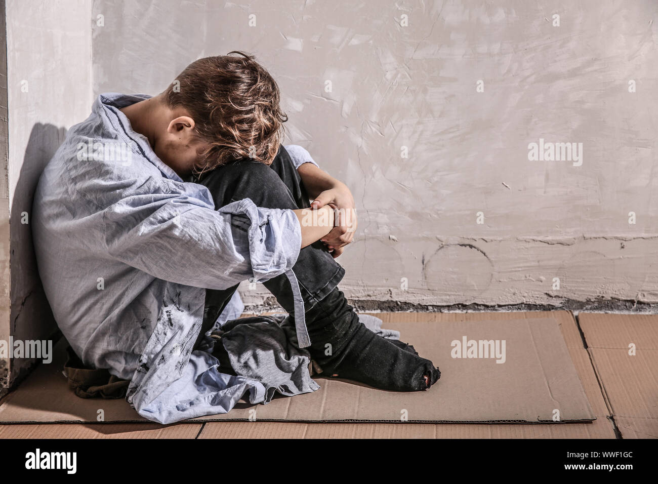 Homeless little boy sitting on floor near wall Stock Photo - Alamy