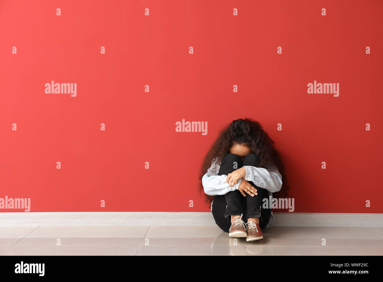 Lonely African-American girl sitting on floor near color wall Stock ...