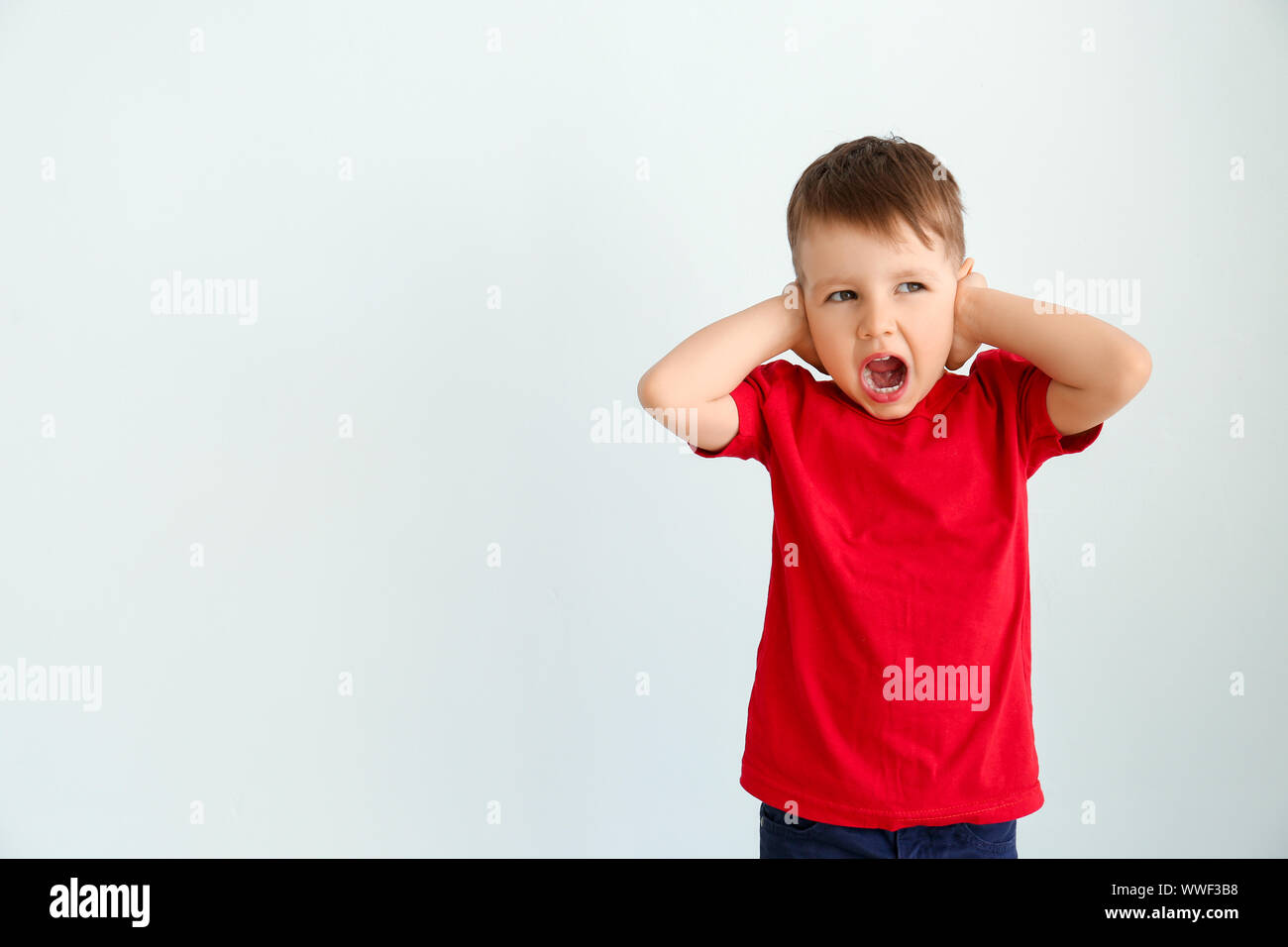 Screaming little boy with autistic disorder covering ears on light ...