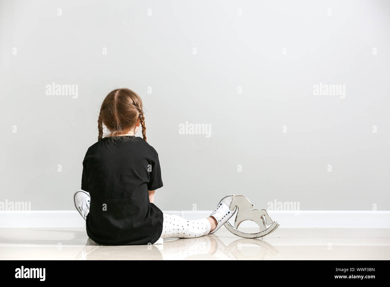 Little girl with autistic disorder sitting on floor near grey wall ...