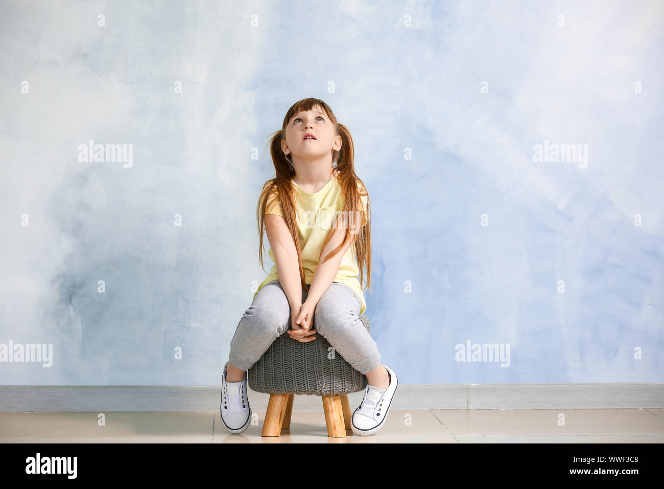 Little girl with autistic disorder sitting near light wall Stock Photo ...