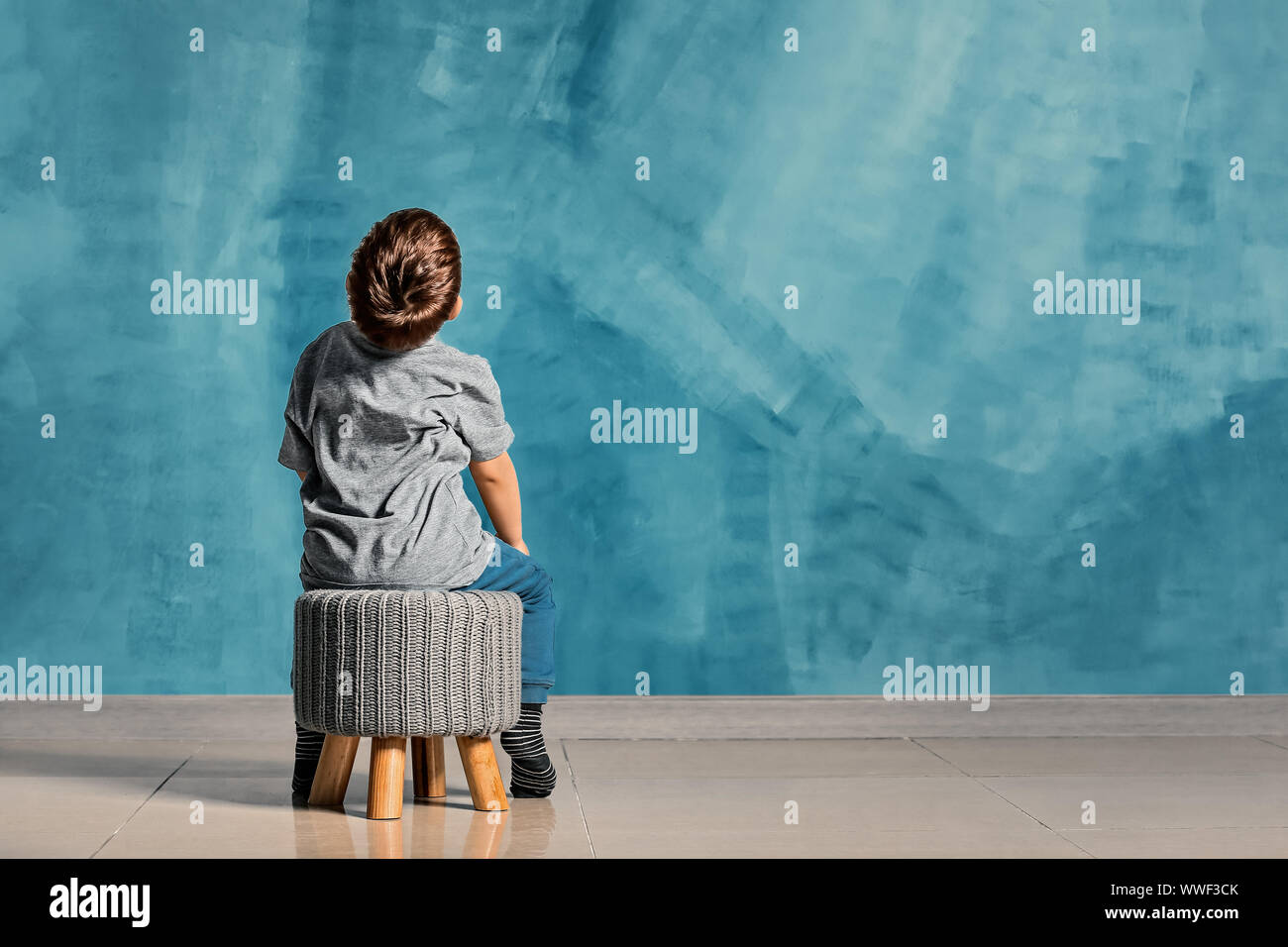 Little boy with autistic disorder sitting near light wall, back view ...