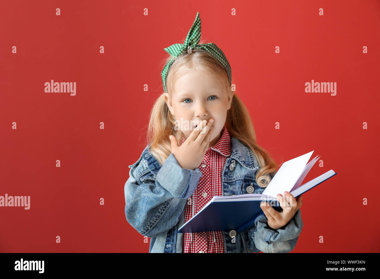 Portrait of surprised little girl reading book on color background ...
