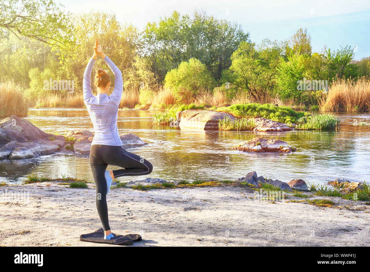 Beautiful young woman practicing yoga near river Stock Photo - Alamy