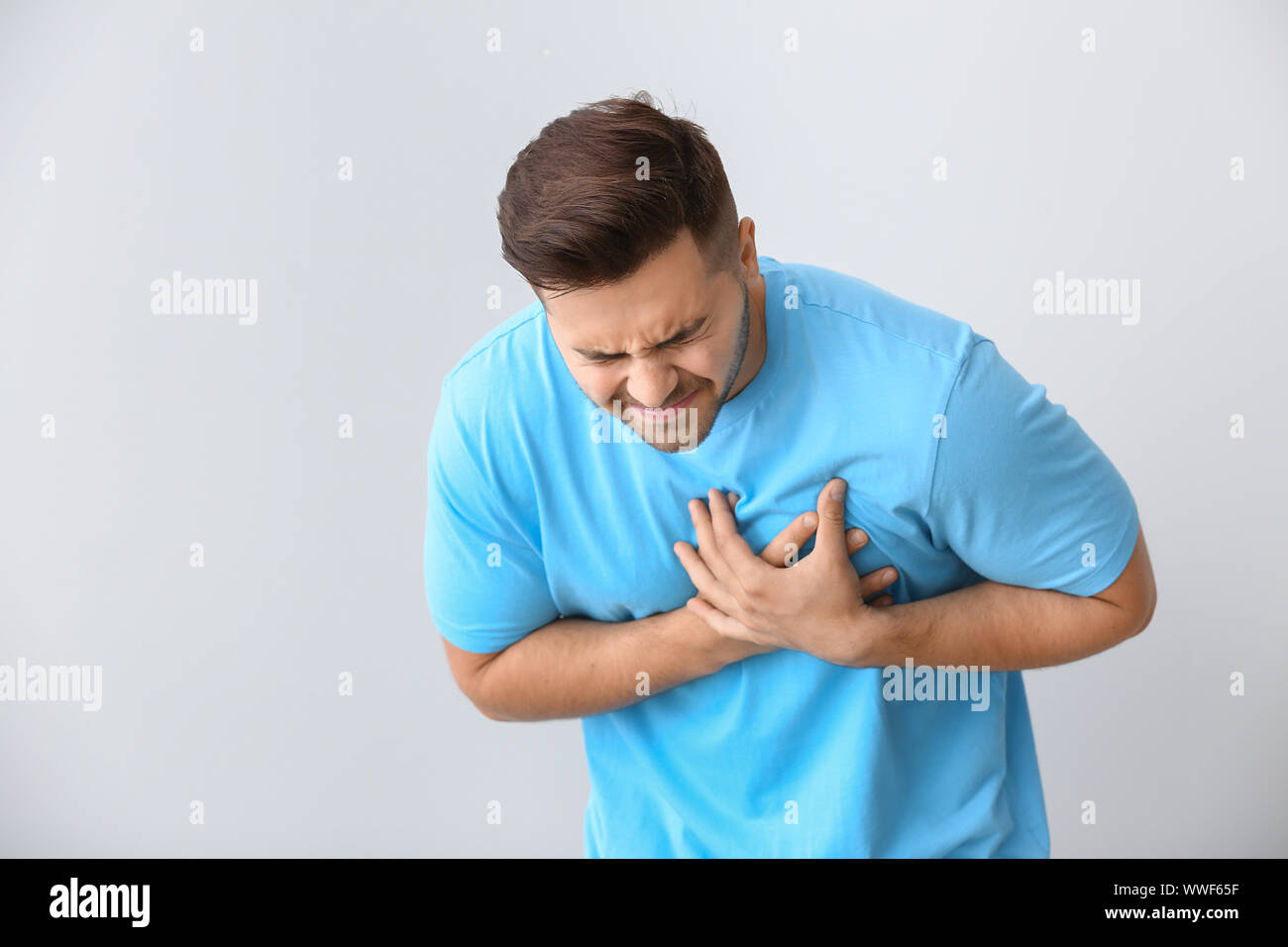 Young man suffering from heart attack on light background Stock Photo ...