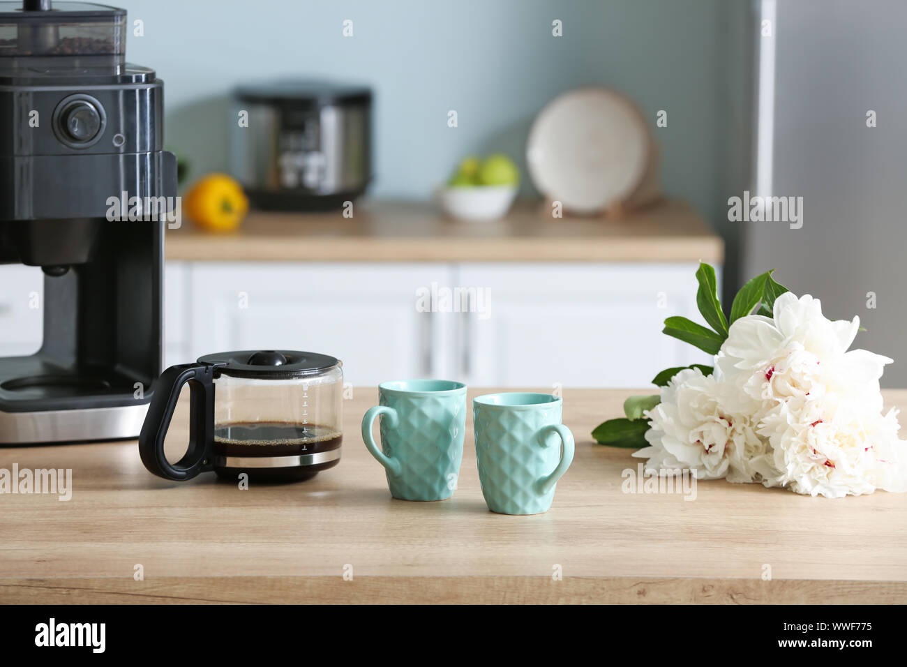 Modern coffee machine with cups and flowers on table in kitchen Stock ...