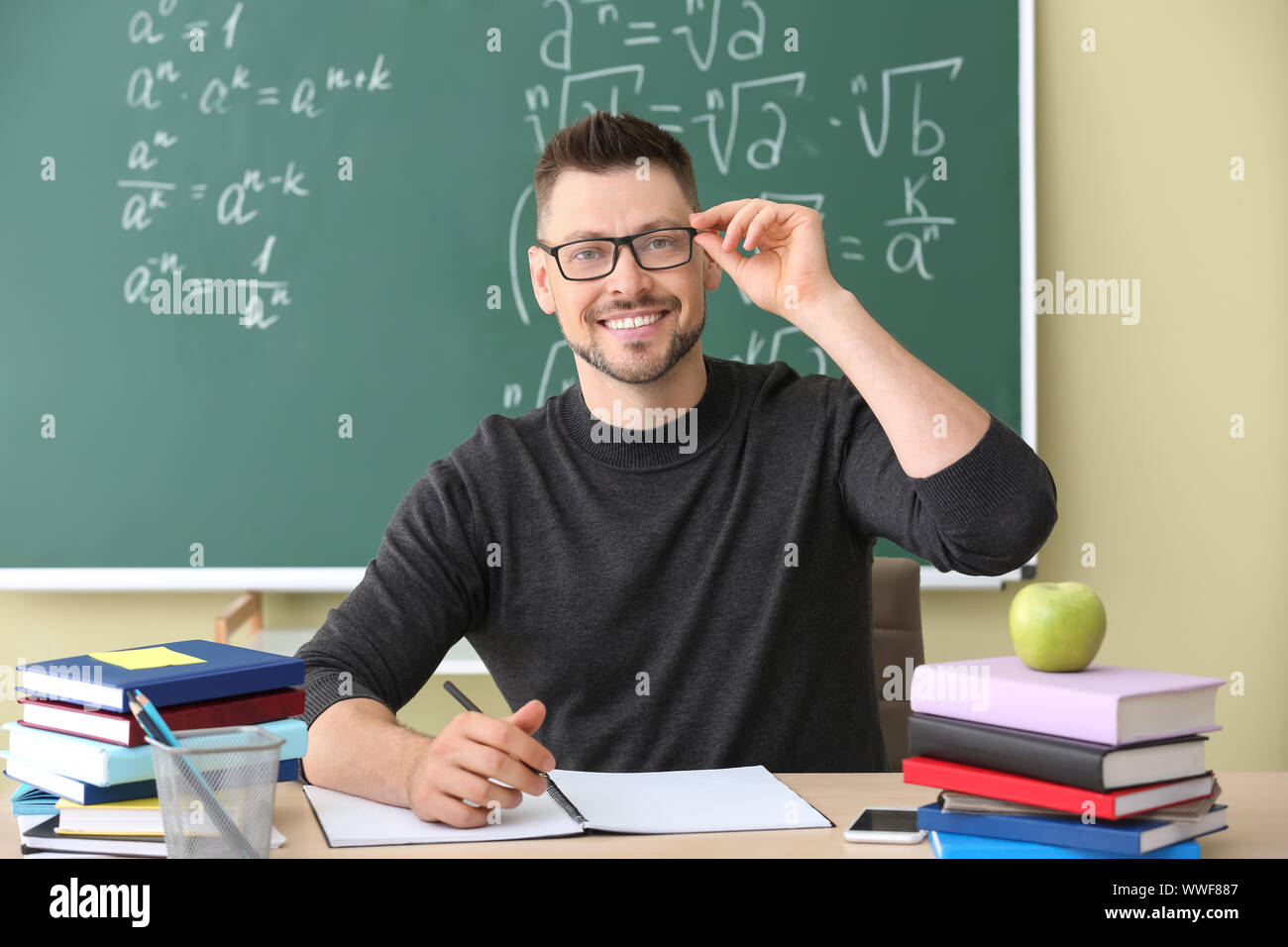 Handsome math teacher sitting at table in classroom Stock Photo - Alamy