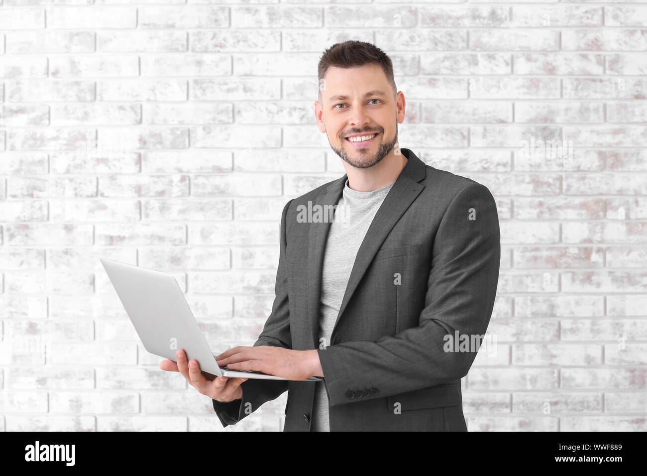 Handsome male teacher with laptop near brick wall Stock Photo - Alamy