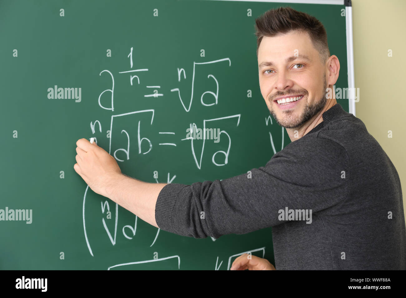 Handsome math teacher writing on blackboard in classroom Stock Photo ...