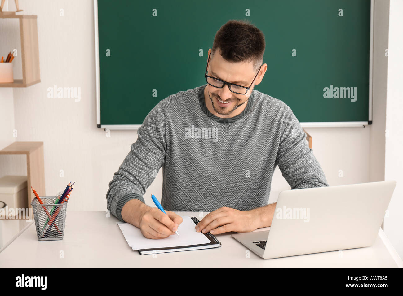 Handsome male teacher with laptop in classroom Stock Photo - Alamy