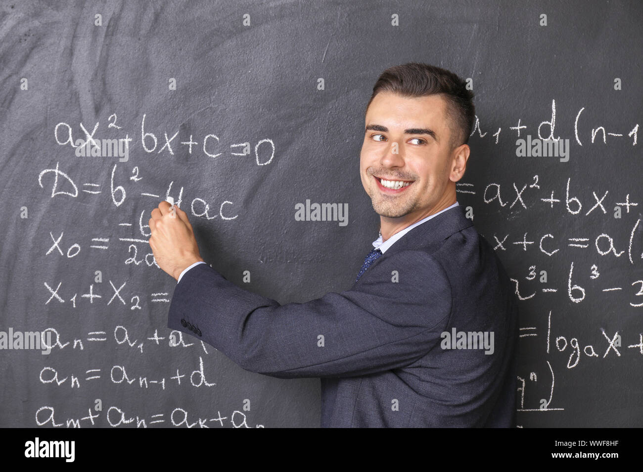 Handsome math teacher writing on blackboard in classroom Stock Photo ...