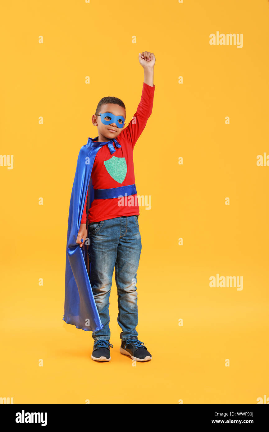 Cute African-American boy dressed as superhero on color background ...